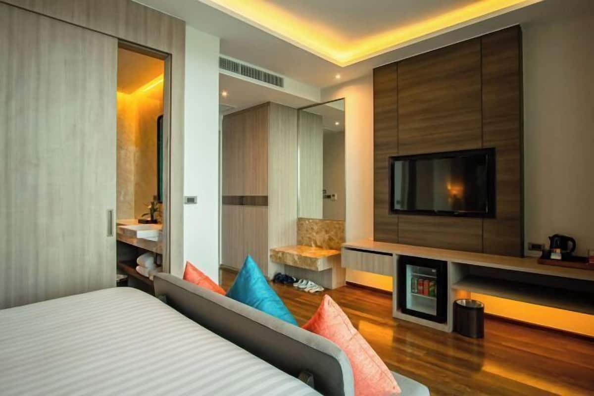 Quarto de hotel moderno com uma cama grande, televisão, um espaço de estar pequeno e minibar.