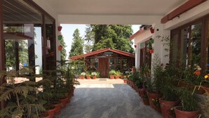 Uma galeria coberta com vasos de plantas que leva a um edifício com telhado vermelho.
