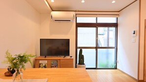 Uma sala de estar moderna com televisão de tela plana, móveis de madeira, um vaso com planta e uma janela grande com vista para a cidade.