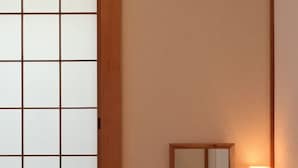 Um quarto japonês tradicional com tatames, um biombos shoji, uma pequena mesa de madeira com um espelho e um abajur, além de uma planta em vaso.