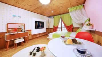 Quarto acolhedor com cama, televisão, escrivaninha com cadeira e área de refeições com mesa posta para dois.