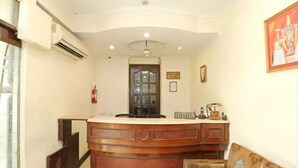 Uma área de recepção com um balcão de madeira, um sofá, uma moldura com imagem e uma porta com placa em cima.