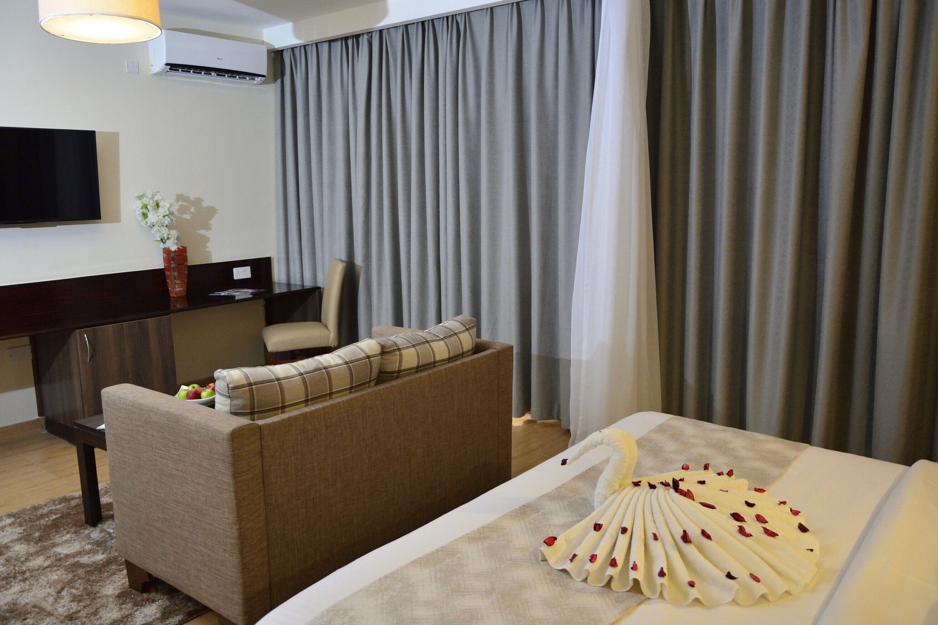 Quarto de hotel com cama, sofá, escrivaninha e televisão.