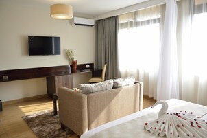 Quarto de hotel com cama, sofá, televisão, escrivaninha e janela com cortinas.