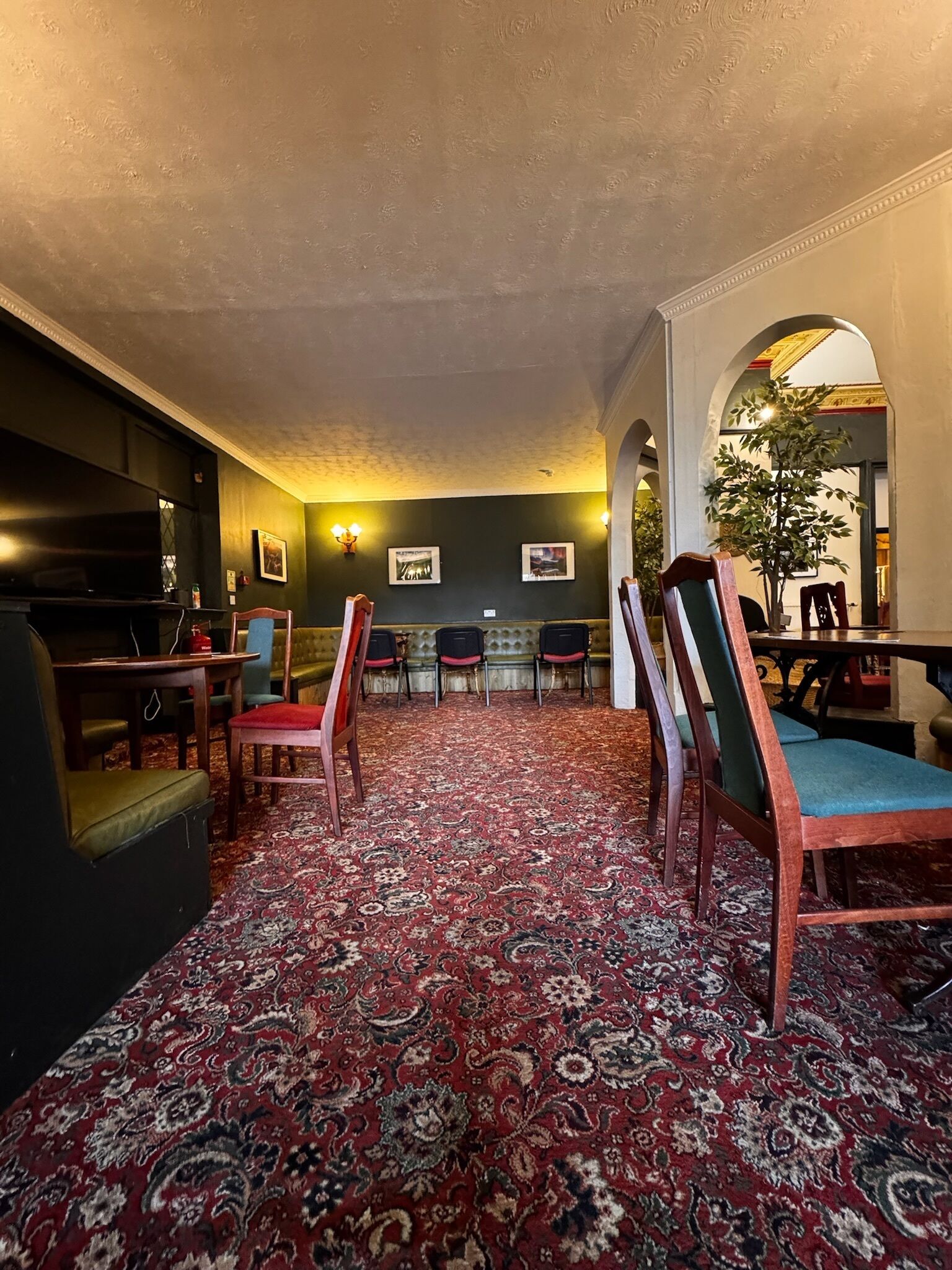 Um quarto com carpete estampado, cadeiras de madeira, um piano e quadros nas paredes.