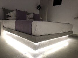 Uma cama moderna com estrutura embutida e iluminação sob a cama, cabeceira e luminária pendente.