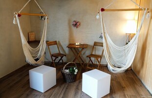 Quarto com duas redes, cadeiras de madeira, uma mesinha com uma vela e cubos brancos de armazenamento.