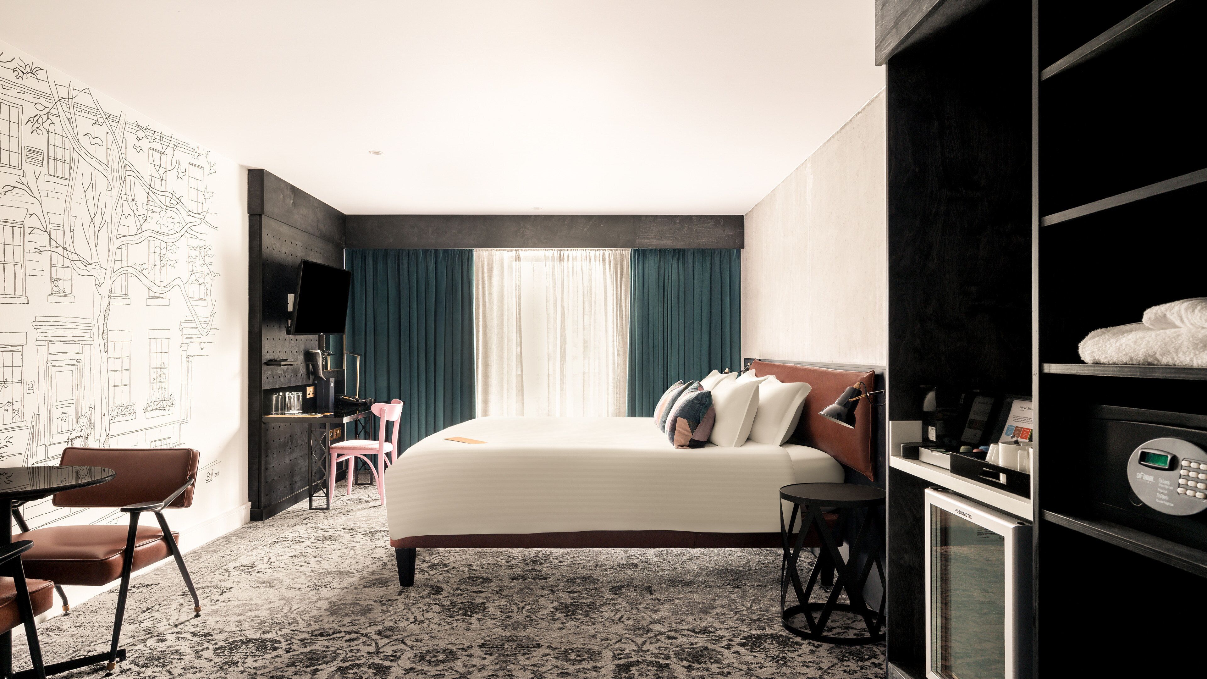 Quarto de hotel moderno com uma cama grande, uma mesa com cadeira, televisão e minibar.