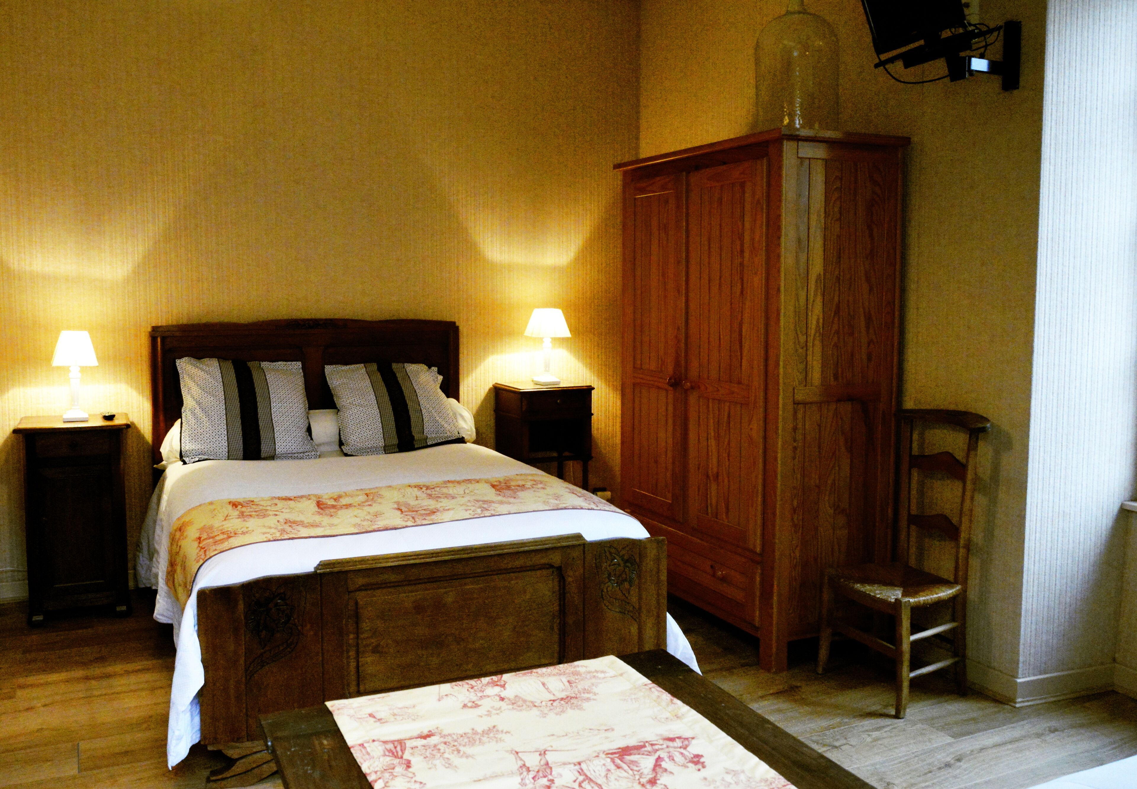 Quarto com cama de madeira, duas luminárias de cabeceira, guarda-roupa de madeira e uma cadeira.