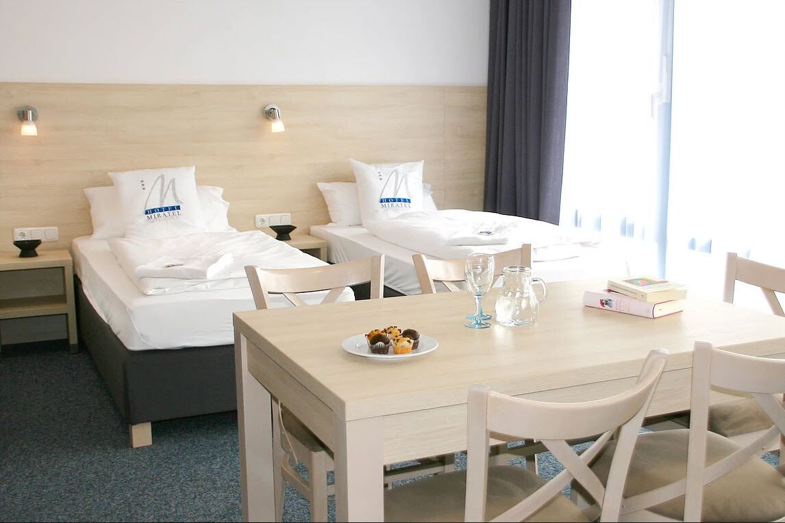 Quarto de hotel com duas camas, uma mesa de jantar e uma mesa pequena com um prato de muffins.