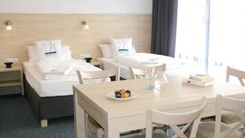 Quarto de hotel com duas camas, uma mesa de jantar e uma mesa pequena com um prato de muffins.