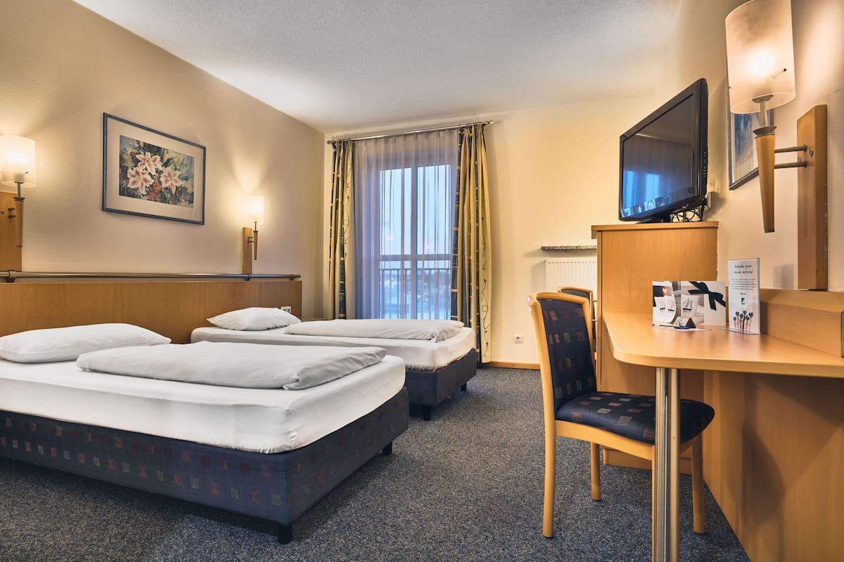Quarto de hotel com duas camas, uma escrivaninha, televisão e uma janela com cortinas.