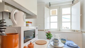 Cozinha moderna com armários brancos, micro-ondas e janela com persianas.