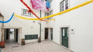 Um pátio com piso de azulejos, uma porta verde e uma parede branca.
