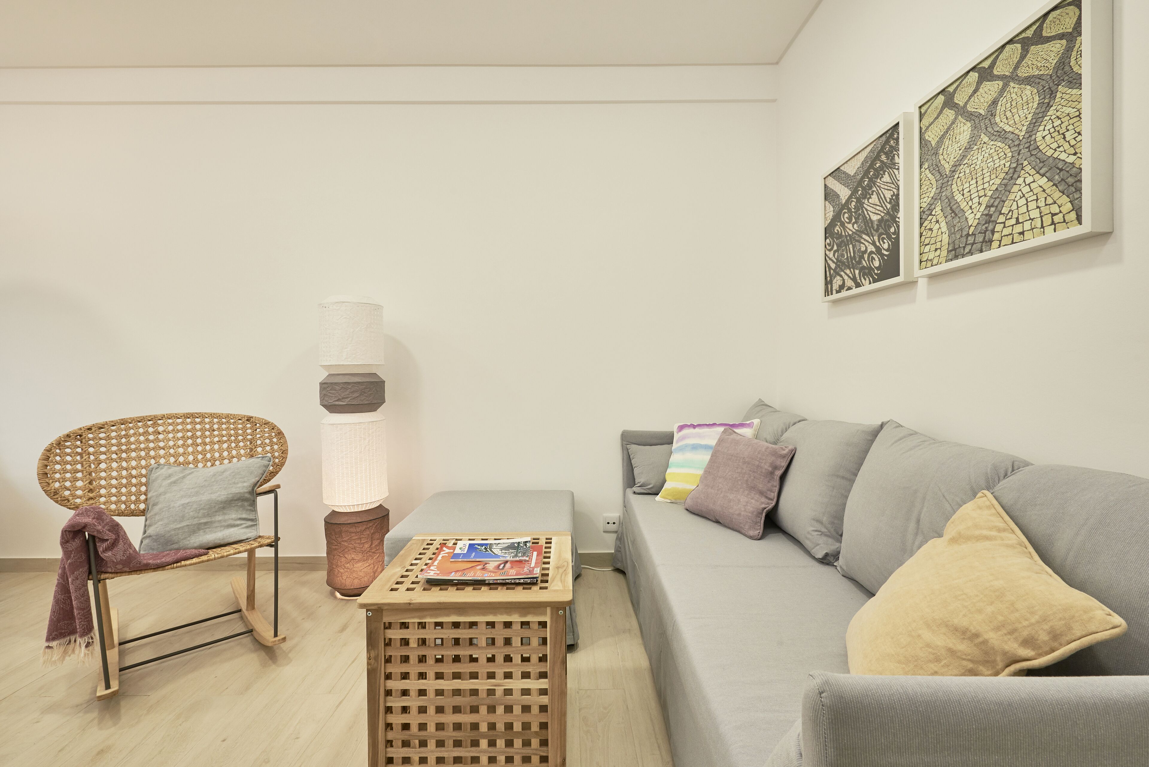 Uma sala de estar moderna com um sofá cinzento, uma cadeira de madeira, uma mesa pequena de madeira e um abajur.
