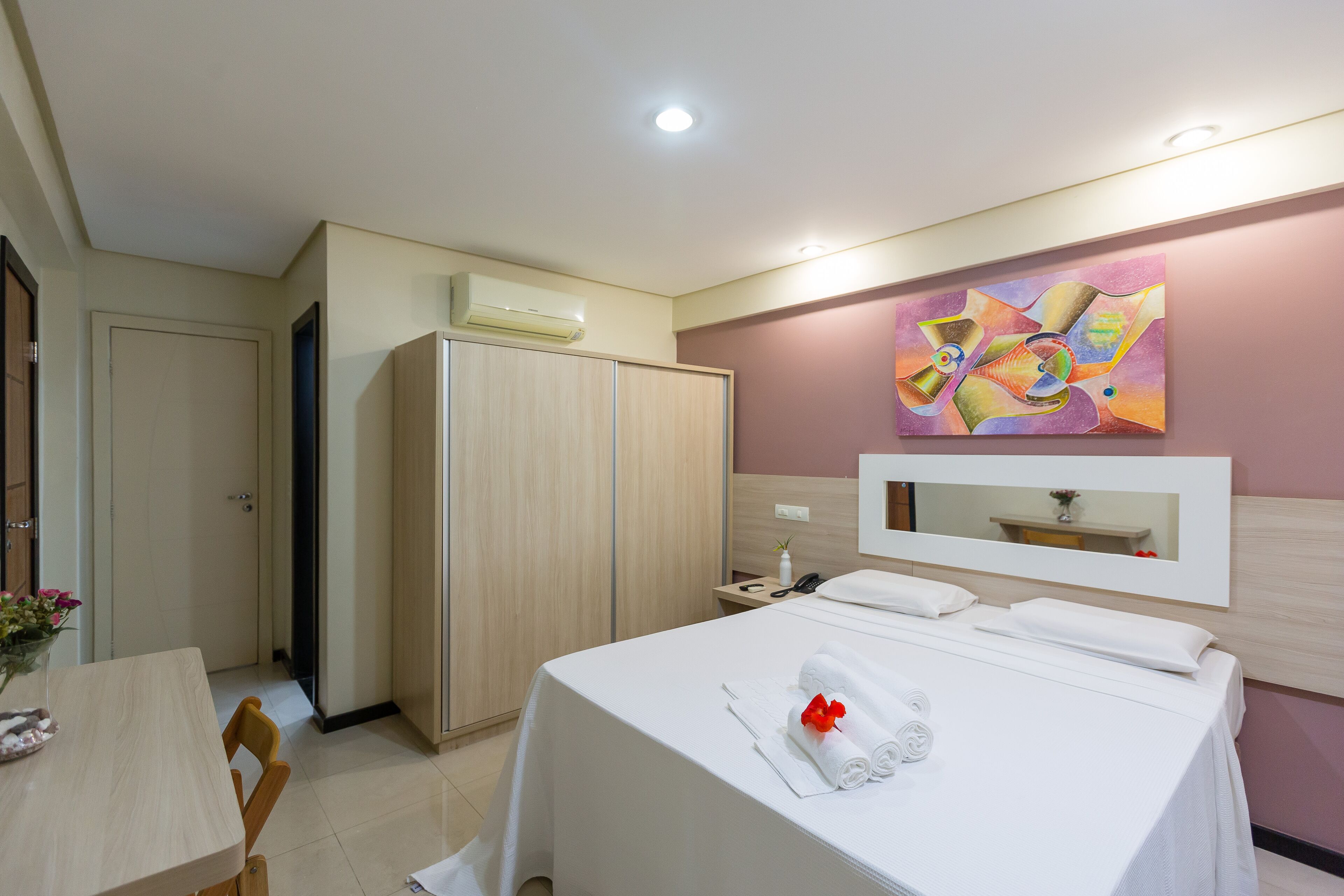 Quarto de hotel com cama, guarda-roupa, escrivaninha e espelho de banheiro.