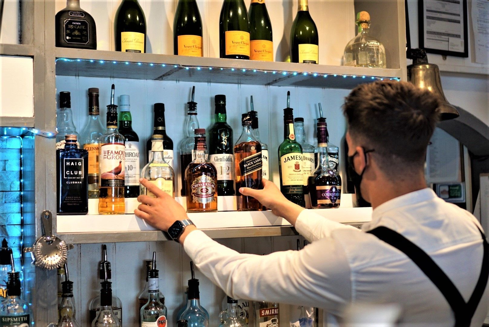 Um barman escolhe uma garrafa numa prateleira de bar bem abastecida.