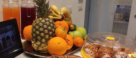 Uma mesa com uma abacaxi, bananas, laranjas, um bolo e um copo de suco de laranja.