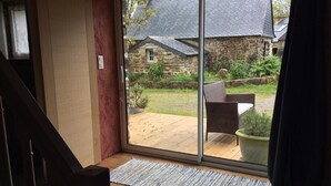 Quarto com piso de madeira, porta de vidro deslizante para um pátio com cadeira de vime e planta em vaso.