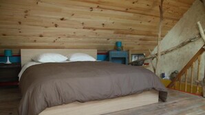 Quarto de cabana de madeira com cama, mesa de cabeceira e abajur.