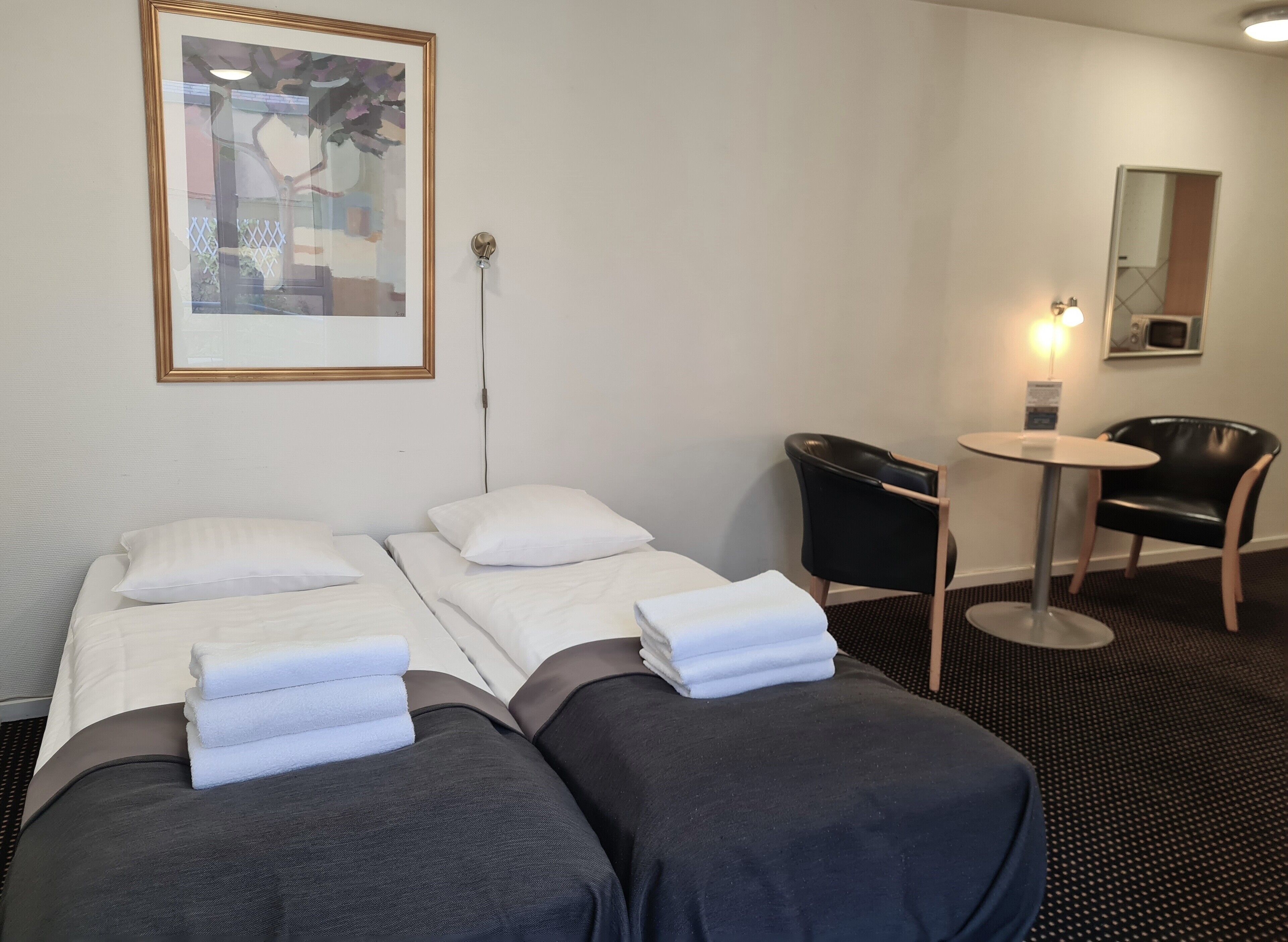 Quarto de hotel com duas camas, uma mesinha, uma cadeira e um quadro na parede.