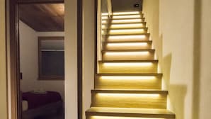 Uma escadaria de madeira com iluminação embutida, conduzindo a um quarto com uma cama e uma janela.