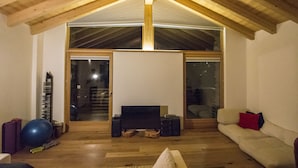 Uma sala de estar com teto de madeira, televisão, sofá e uma janela grande.