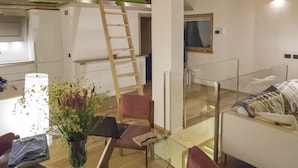 Um amplo loft com teto alto, vigas de madeira, uma mesa de jantar de vidro e uma área de estar confortável.