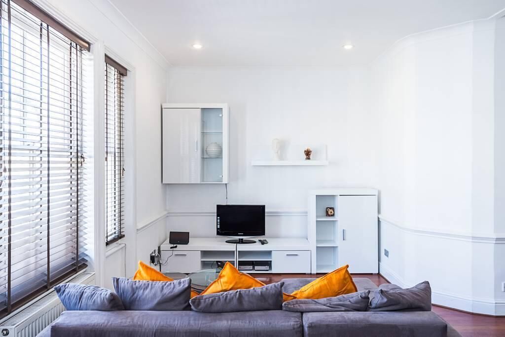 Uma sala de estar moderna com um sofá cinzento, uma TV de tela plana e um rack branco.