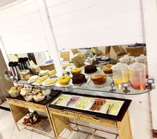Buffet com diversos alimentos e bebidas expostos em um balcão de vidro.