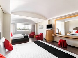 Quarto de hotel com duas camas, televisão, escrivaninha e espelho.
