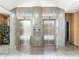 Elevador moderno com paredes de granito e chão de mármore numa área de recepção.