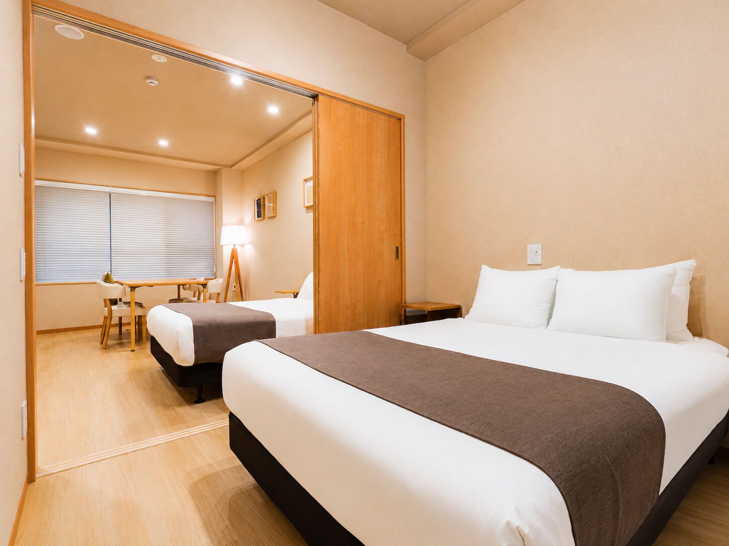 Quarto de hotel com uma cama grande, uma cama menor, uma escrivaninha e uma cadeira.