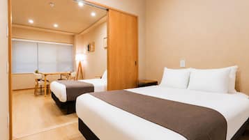 Quarto de hotel com uma cama grande, uma cama menor, uma escrivaninha e uma cadeira.