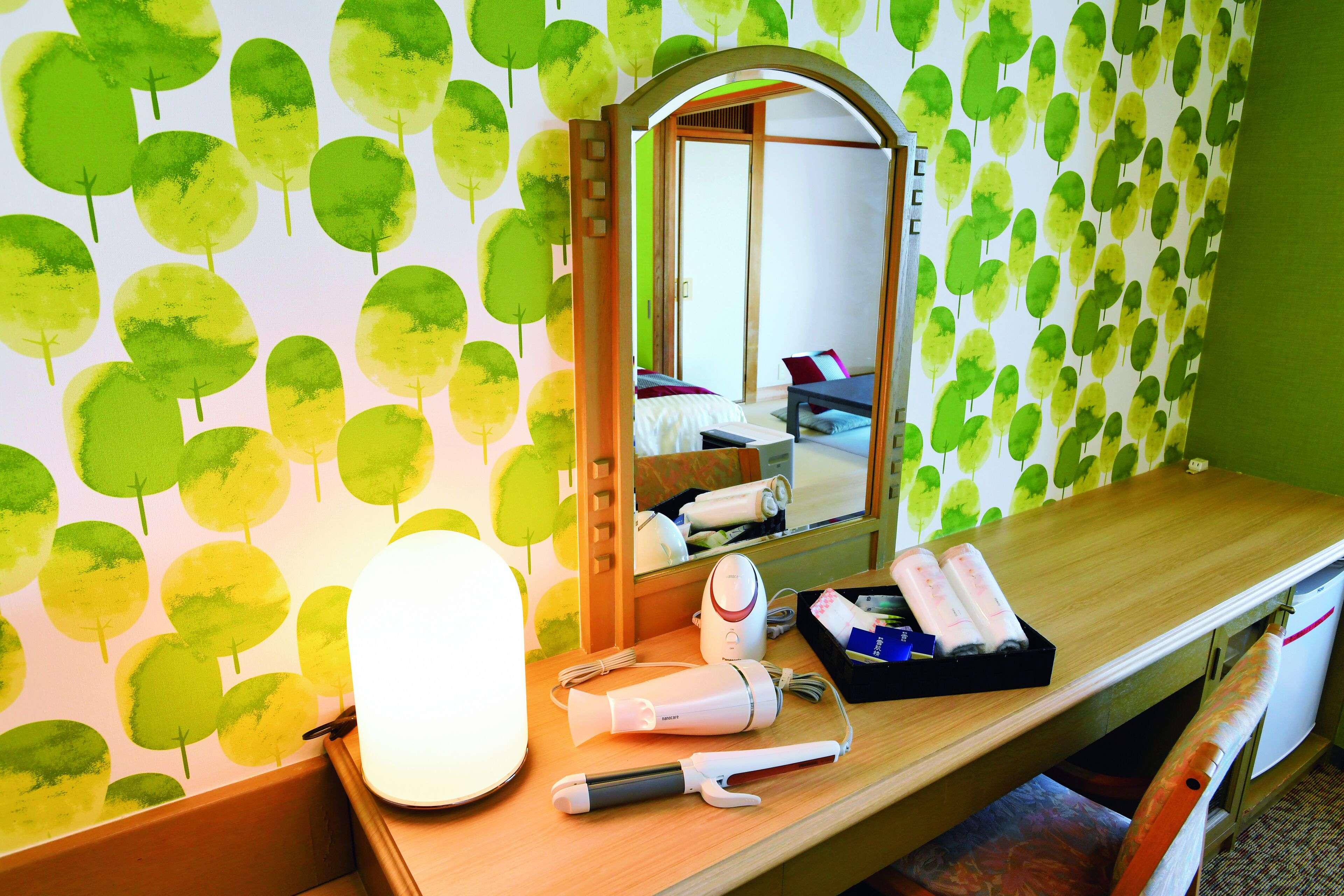 Quarto de hotel com escrivaninha de madeira, espelho e parede com padrão de árvore.