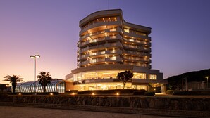 Um hotel com vários andares, fachada curva, varandas em cada andar e entrada de vidro.