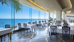 Uma ampla área de refeições com mesas e cadeiras, janelas grandes com vista para o oceano e um design de teto moderno.