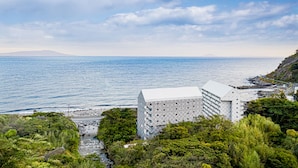 Um hotel costeiro com design moderno, destacando um edifício branco com fachada geométrica, localizado numa encosta verdejante com vista para o mar.
