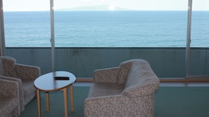 Quarto com vista para o mar, um sofá, uma mesinha e um comando de televisor sobre a mesa.