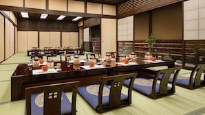 Um quarto tradicional japonês com tatames, uma mesa baixa e cadeiras, e uma janela grande com portas deslizantes.