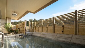 Uma área de piscina interna moderna, com piso de pedra, cercas de madeira e céu claro.