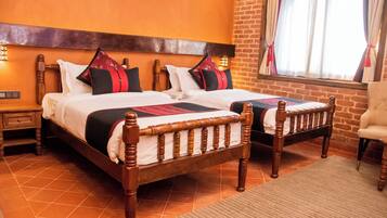 Uma cama de casal com estrutura e cabeceira de madeira, uma mesa de cabeceira e uma cadeira em um quarto com paredes laranja e uma parede em tijolo.