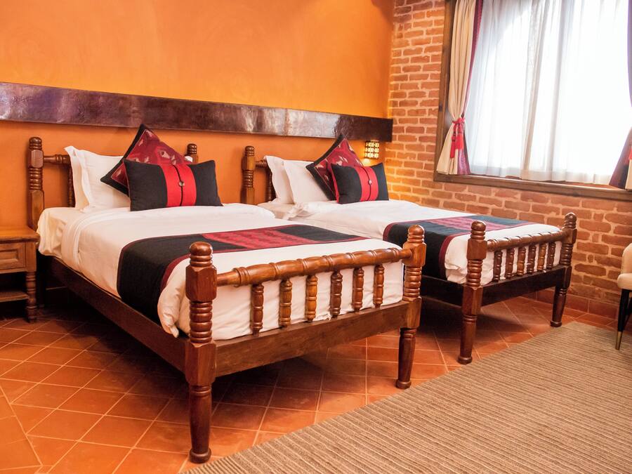 Uma cama de casal com estrutura e cabeceira de madeira, uma mesa de cabeceira e uma cadeira em um quarto com paredes laranja e uma parede em tijolo.