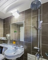 Uma casa de banho moderna com um espelho grande, uma sanita branca, um chuveiro manual e um porta-toalhas.