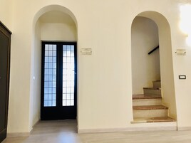 Um corredor com duas portas arqueadas que dão para uma escadaria e uma porta com um vitral fosco.