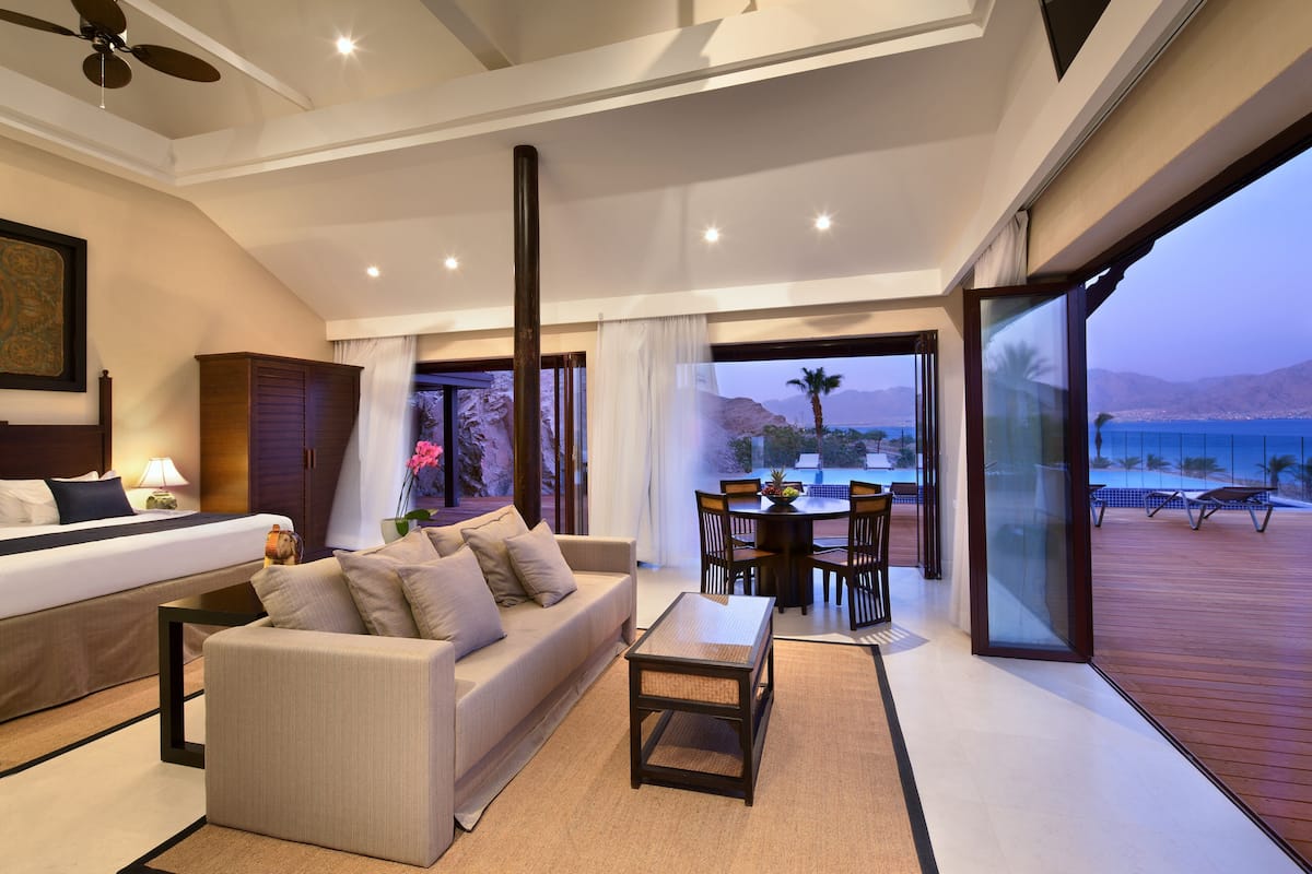Quarto de hotel moderno com varanda, sofá, mesa de jantar e vista para a praia.
