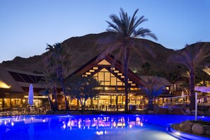 Resort com piscina, área de refeições ao ar livre e um edifício com estrutura de telhado marcante.