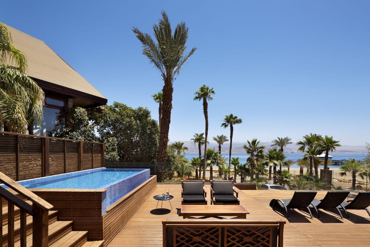 Uma área junto à piscina com espreguiçadeiras, uma mesa pequena e vista para a praia e oceano.