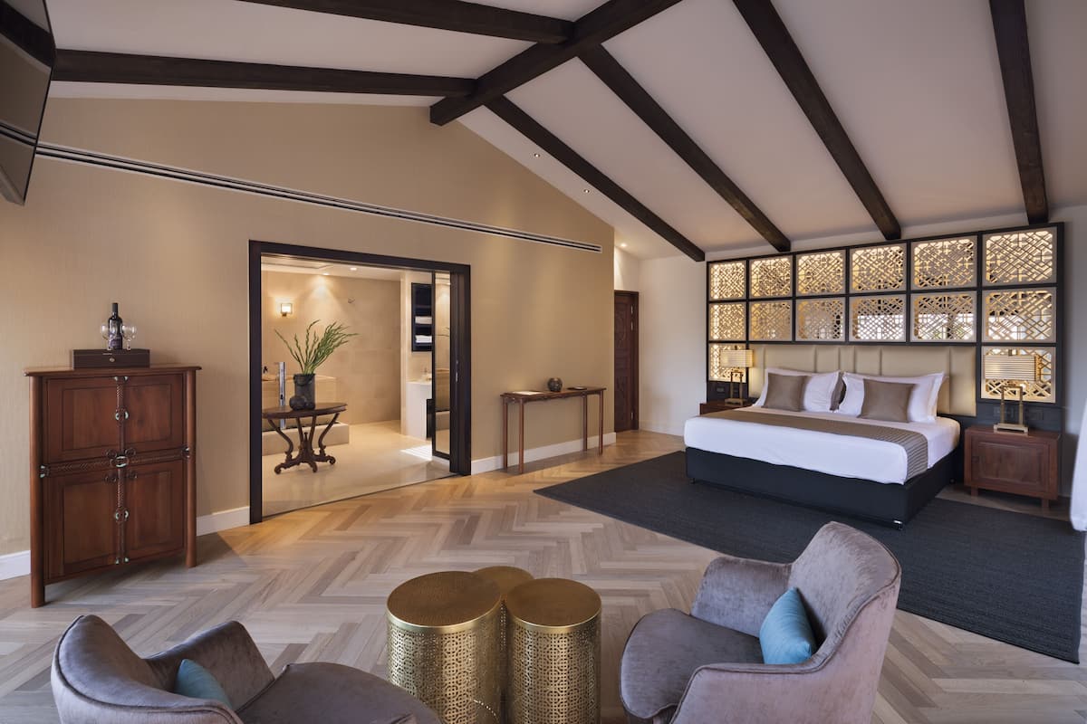 Quarto espaçoso com uma cama grande, guarda-roupa de madeira, área de estar com poltronas e um painel decorativo na parede.