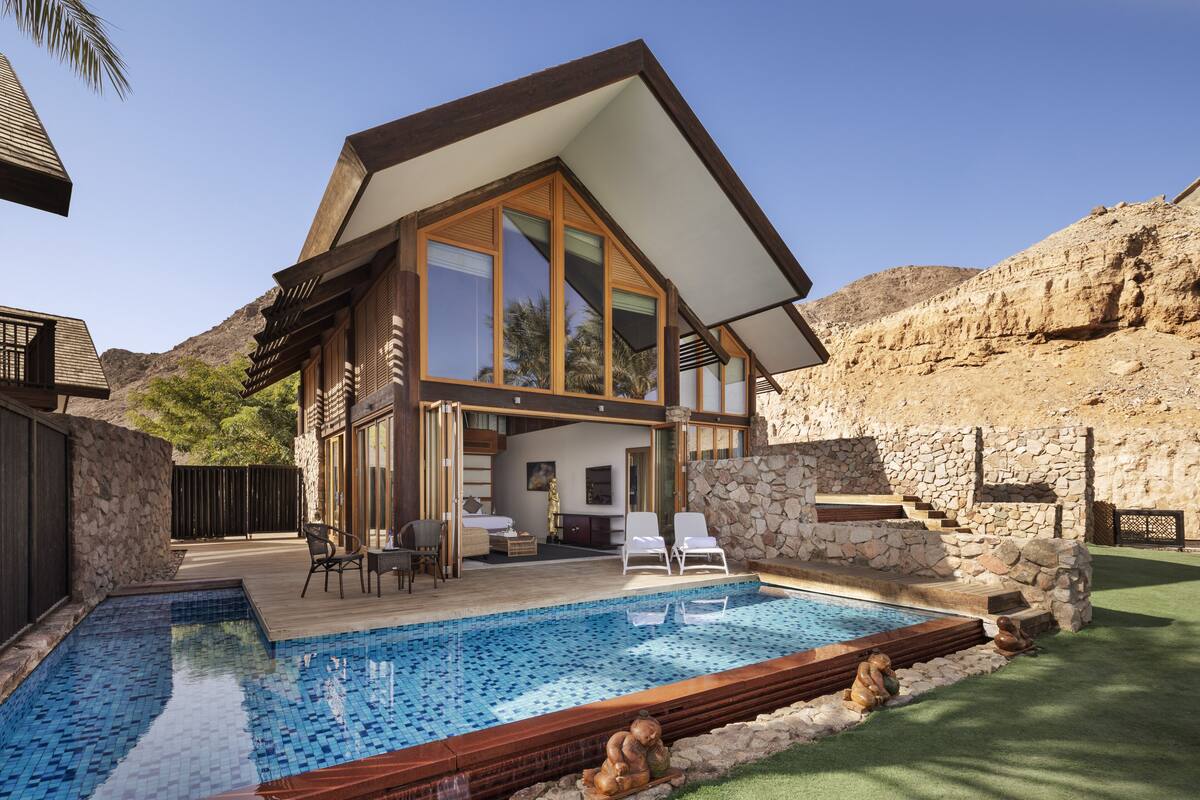 Uma casa moderna com piscina, paredes de pedra e um espaço de estar com espreguiçadeiras.